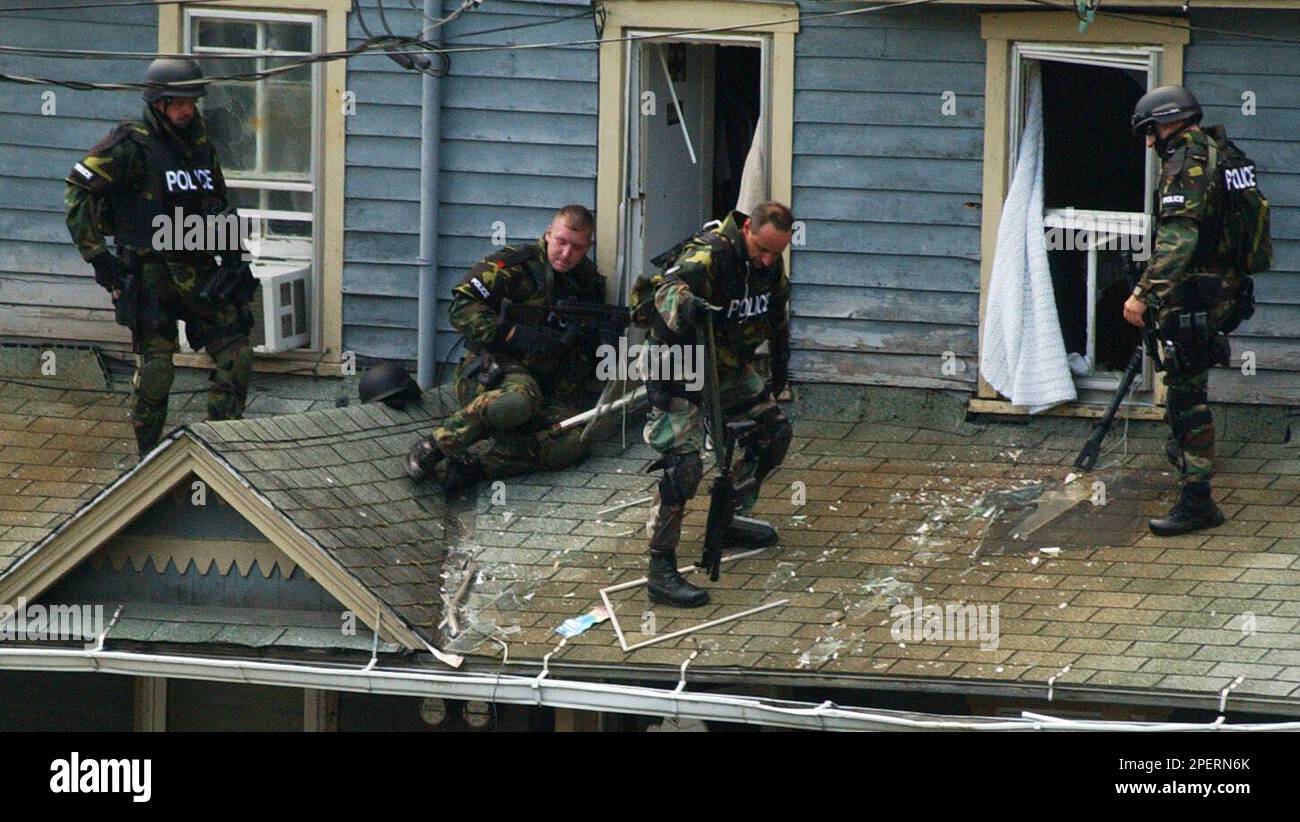 Tactical response police officers stand on the porch roof of a home in ...