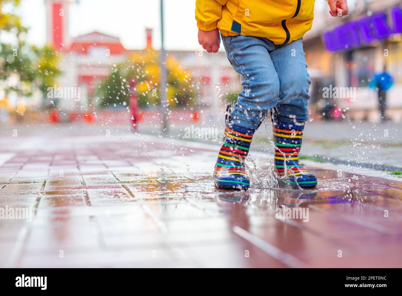 Happy little kid boy jumping on rainy puddle in city street, autumn ...