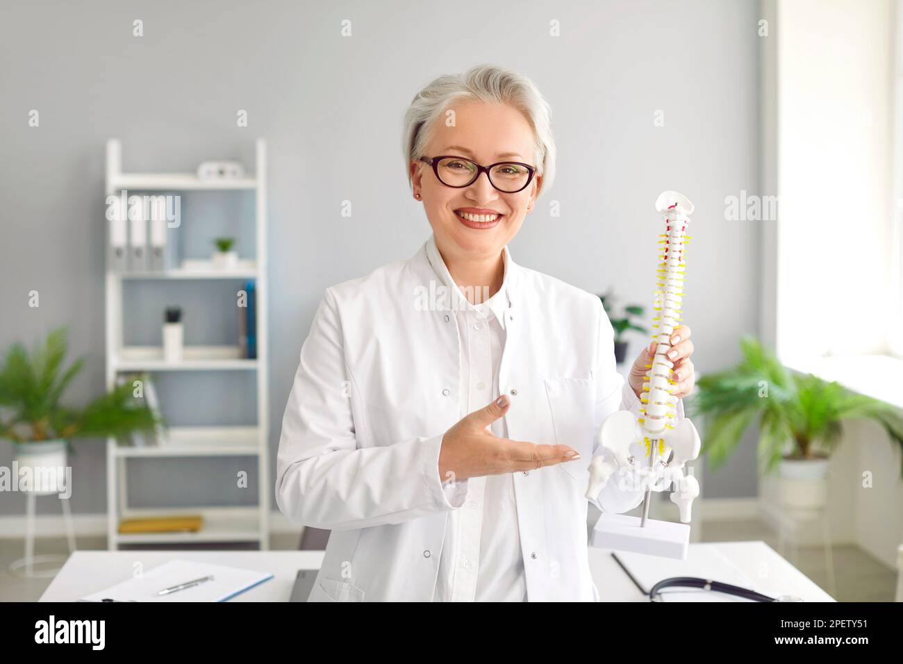 Portrait of happy female doctor holding anatomical model of human spine ...