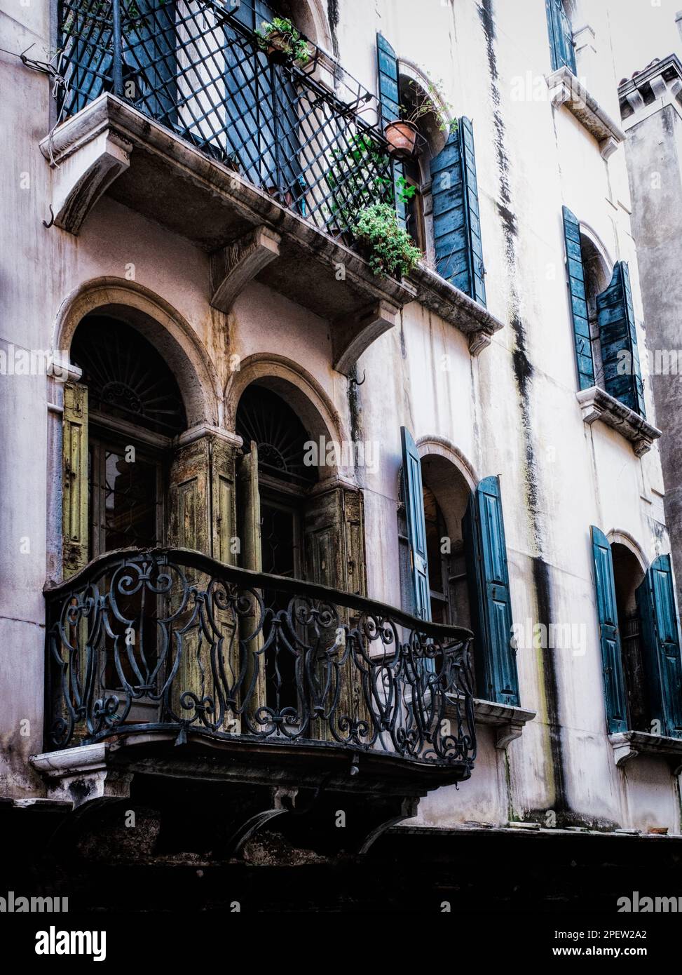 An ornate ironwork balcony and blue shuttered windows in back street of ...