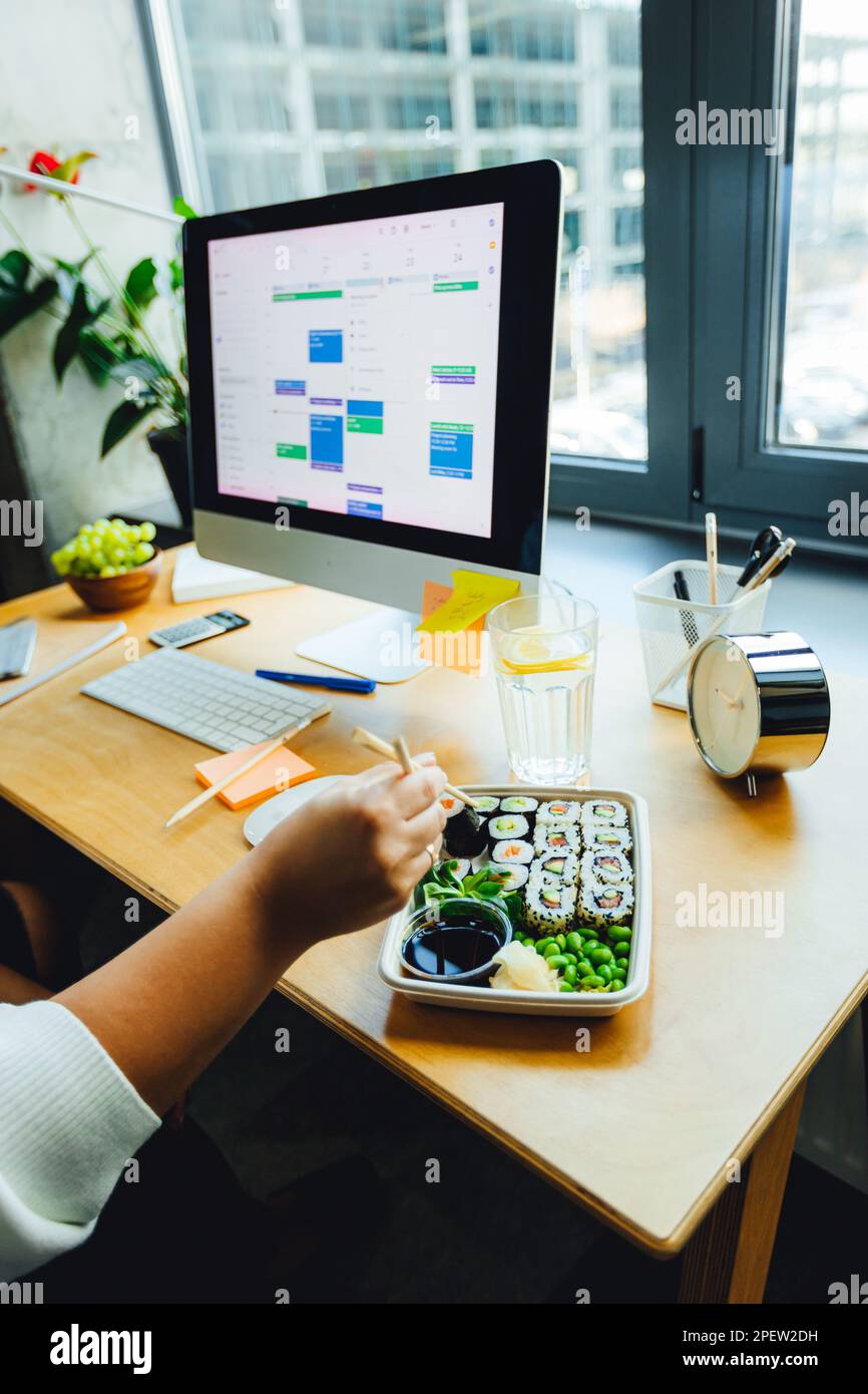 A vertical shot of a woman enjoying takeaway sushi at her office desk ...