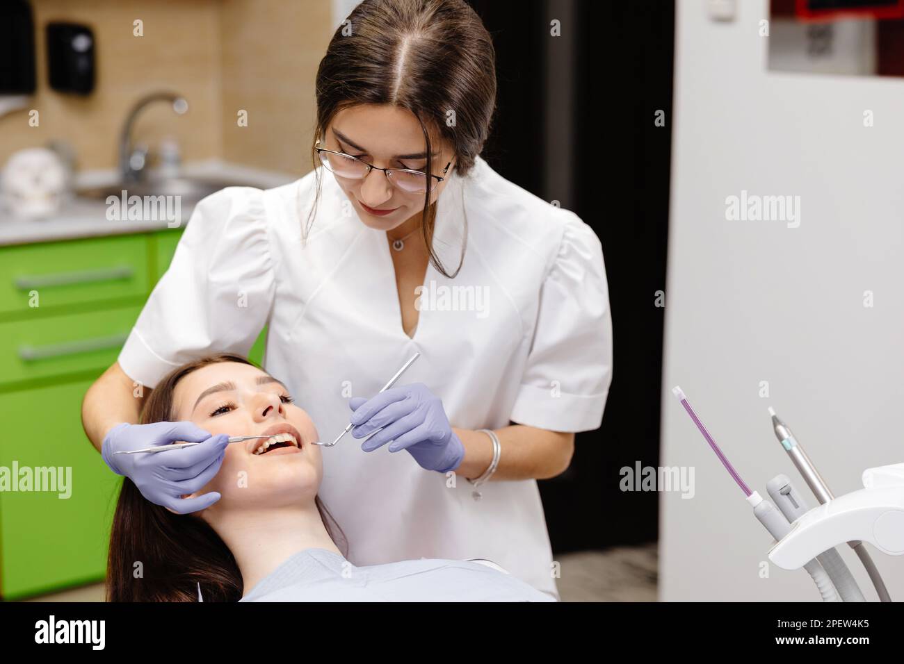 Woman dentist doing treatment for young lady patient, holding dental ...