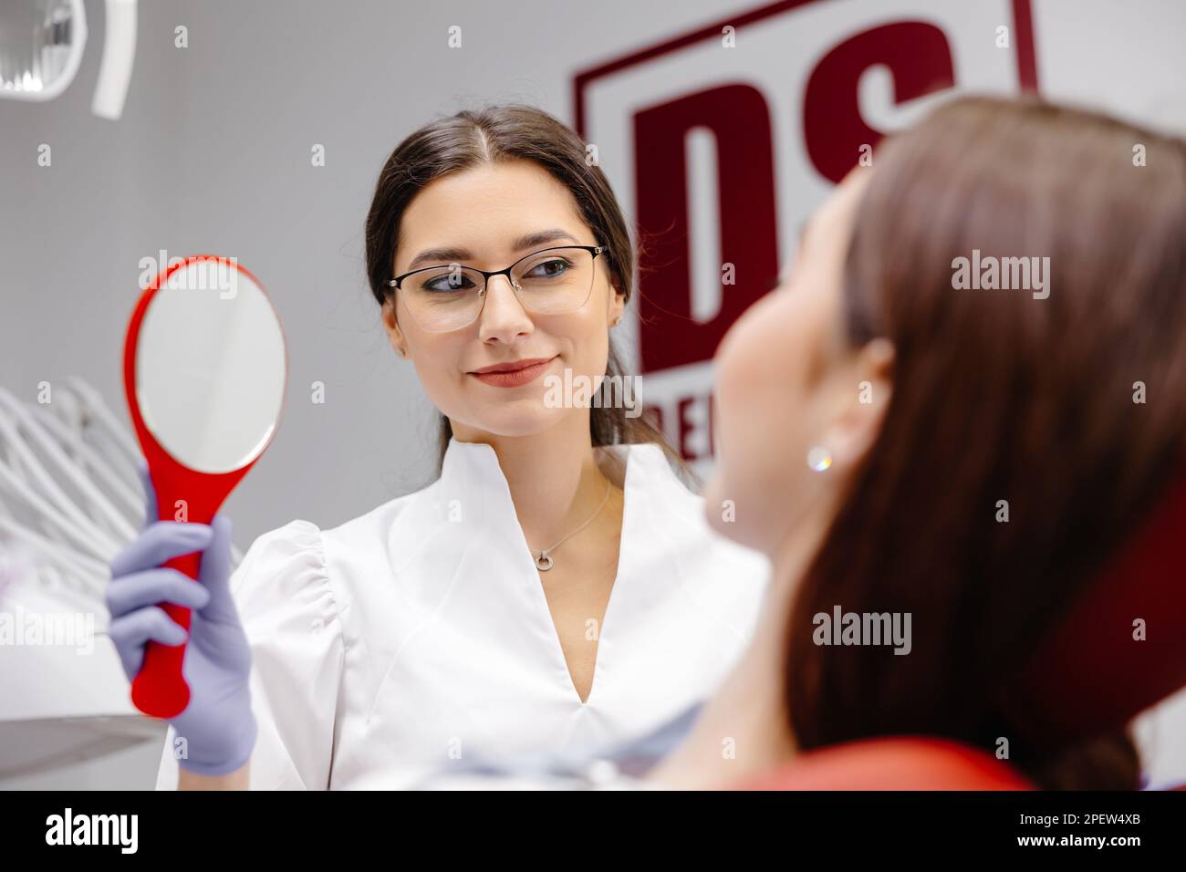 Attractive caucasian lady checking her beautiful smile in mirror after dental treatment. A woman ...