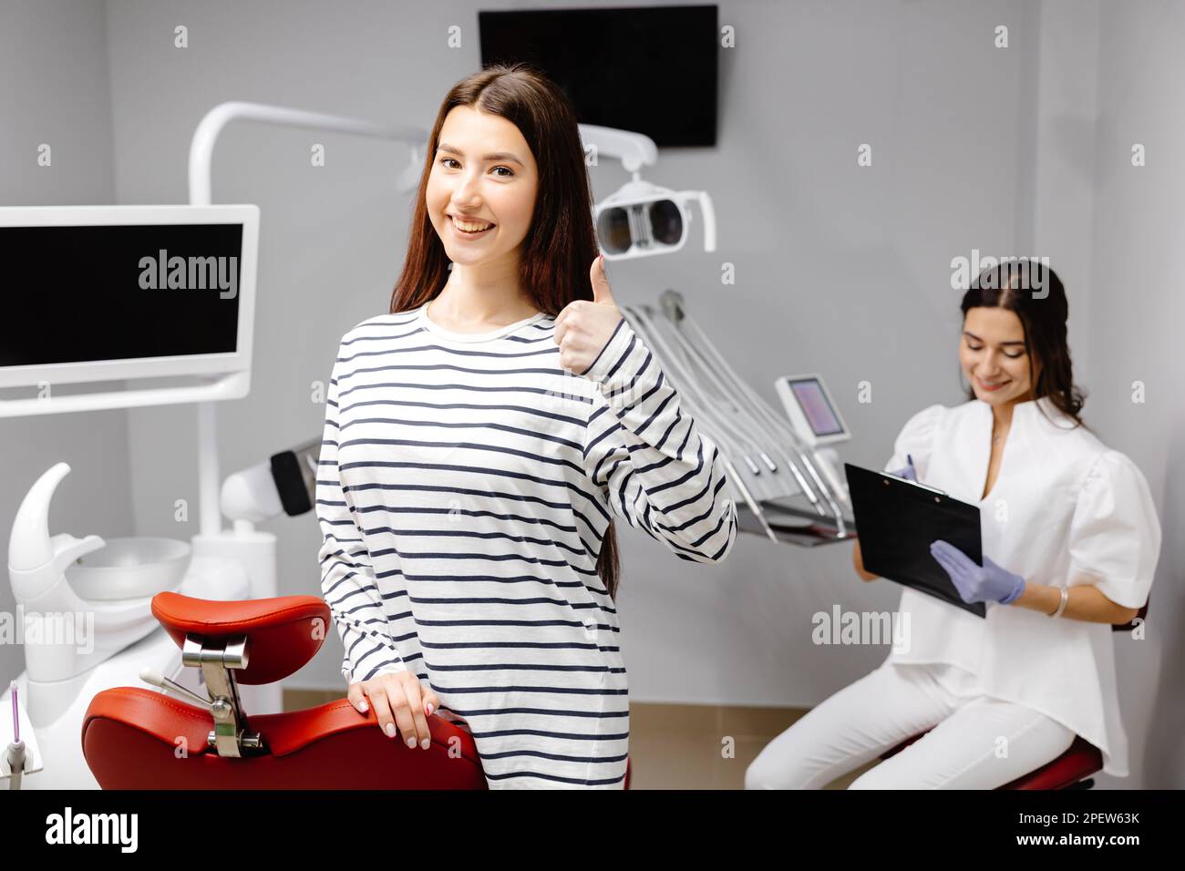 A young girl is standing near the dental chair in the office and is ...