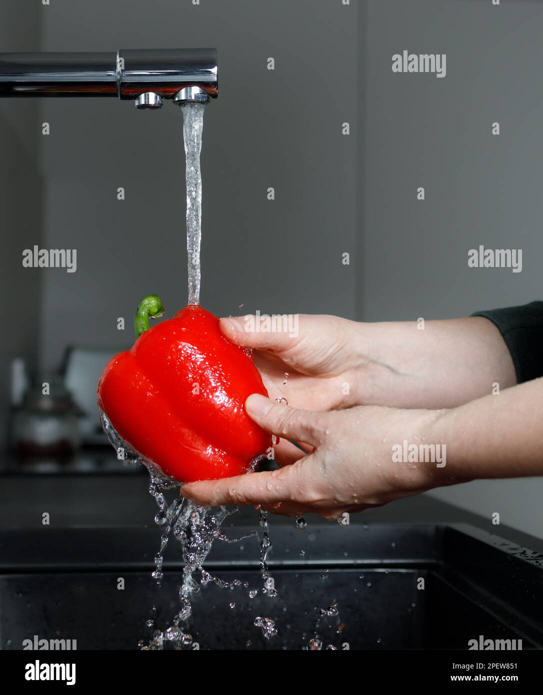 Fresh red pepper under water stream in sink, woman in the kitchen ...