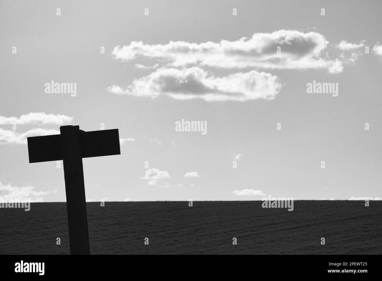 A grayscale of a wooden cross standing amidst a vast and serene field ...