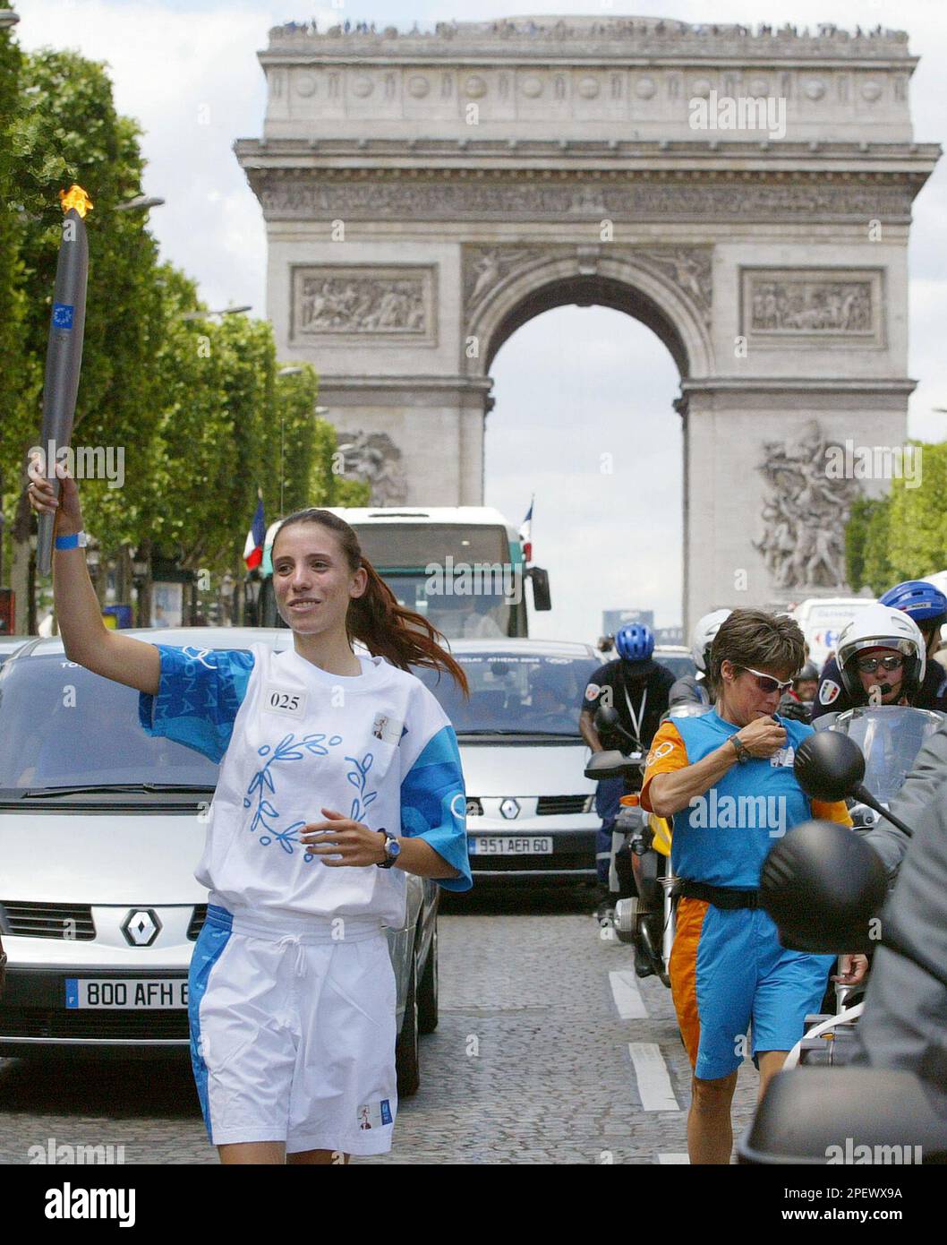 An unidentified runner carries the Olympic Flame past the Arc de ...
