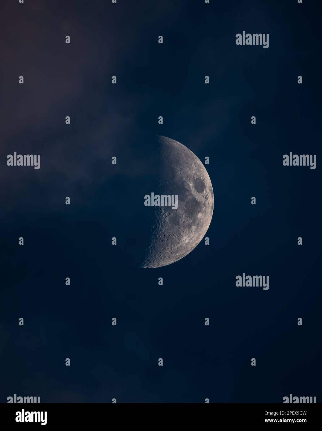 A large half moon partially obscured by clouds in the night sky with a ...