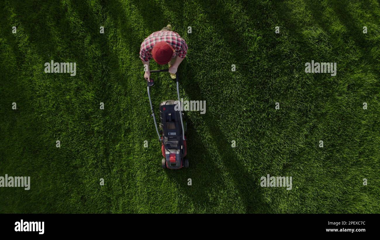 Professional worker with lawn mower mows the grass, top view. Copy ...