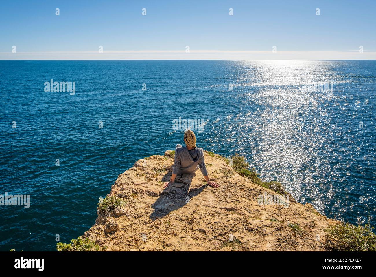 Back of young woman sitting on the top of cliffs immersed in the beauty ...