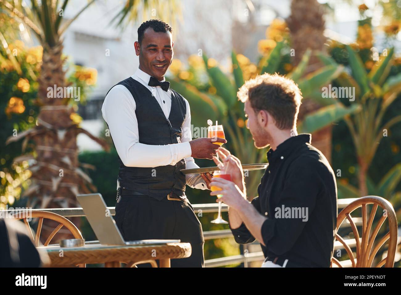Serviced by waiter. Young man is outdoors at sunny daytime. Concept of ...