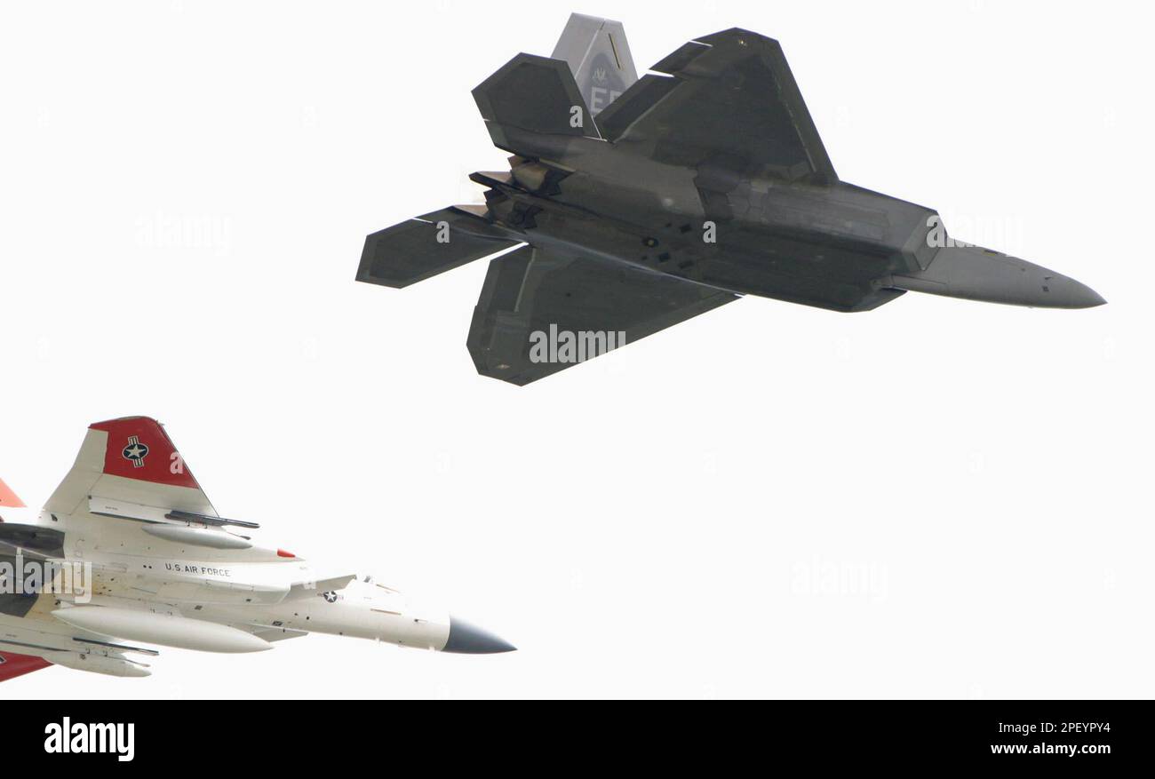A F/A-22 Raptor, painted gray, flies with the older F-15 over Boeing ...