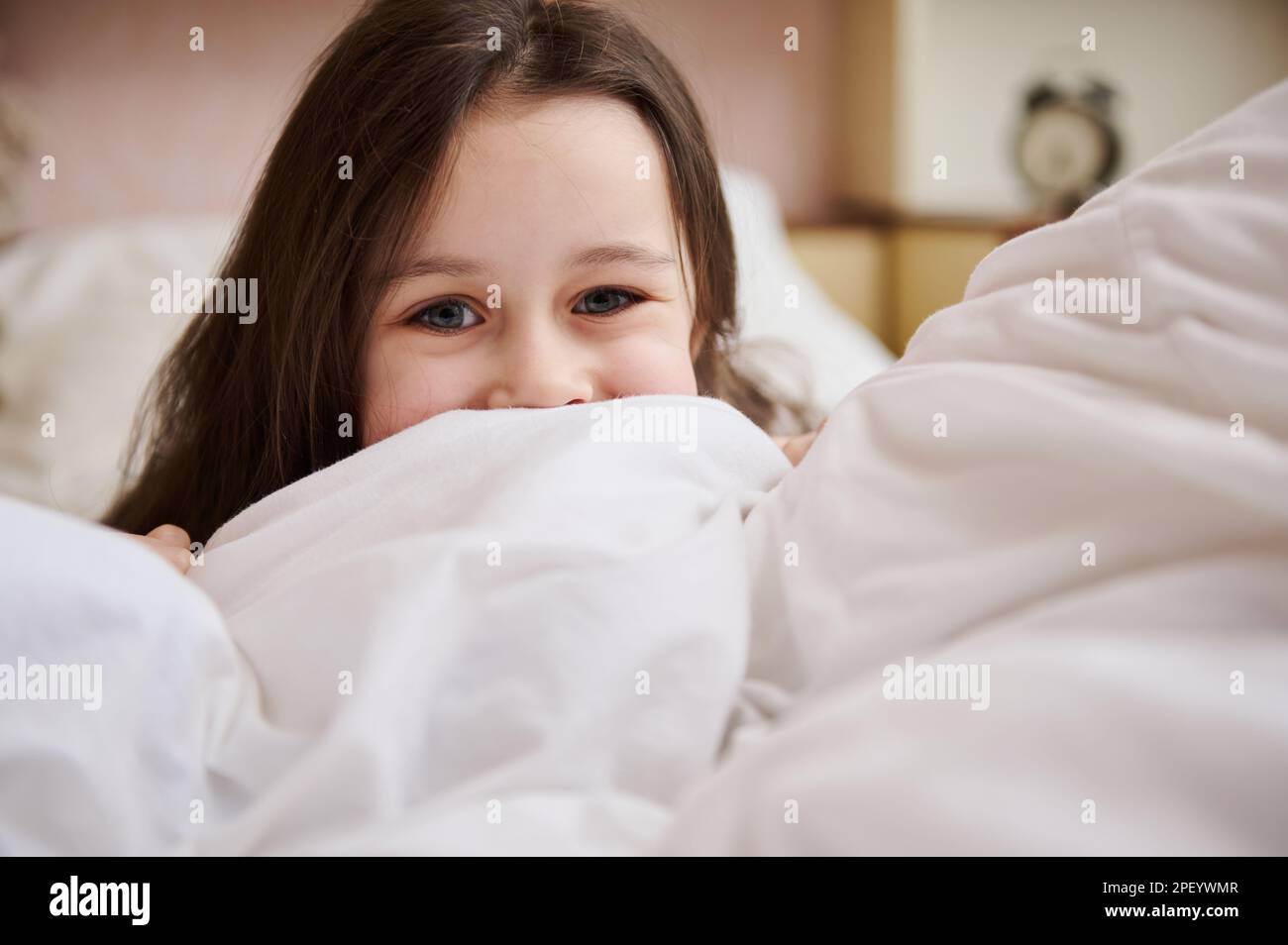Close-up portrait of a happy little child girl lying on comfortable bed ...