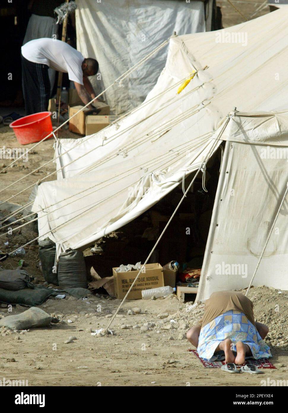 A detainee prays outside his tent in an outdoor detention center in the ...