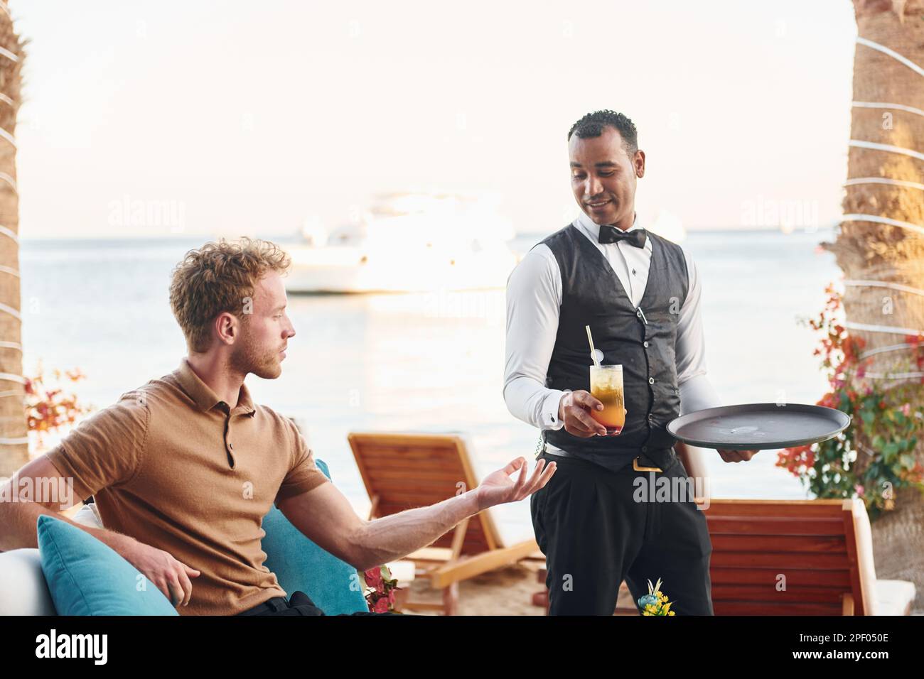 Serviced by waiter. Young man is outdoors at sunny daytime. Concept of ...