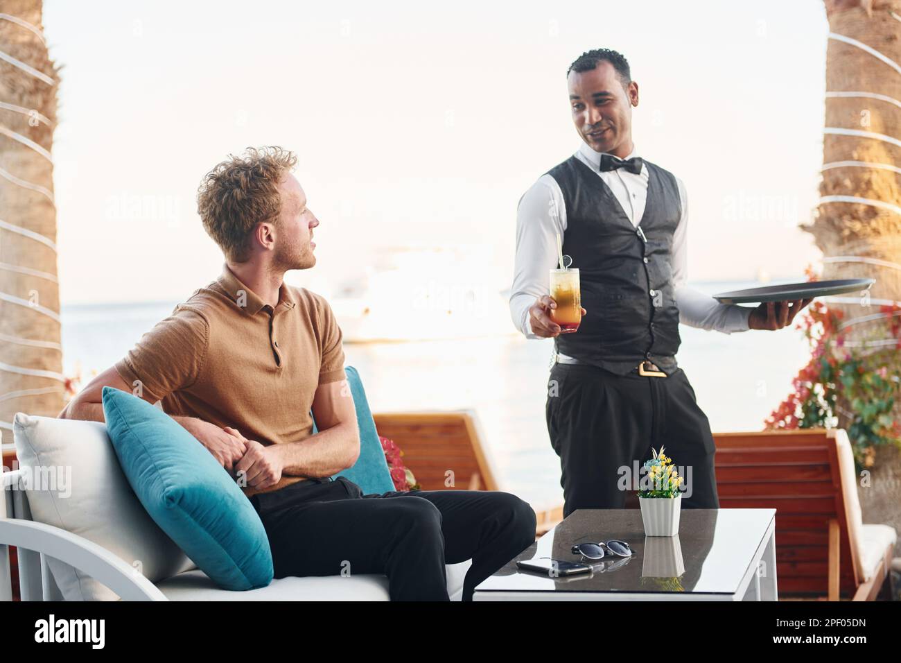 Serviced by waiter. Young man is outdoors at sunny daytime. Concept of ...