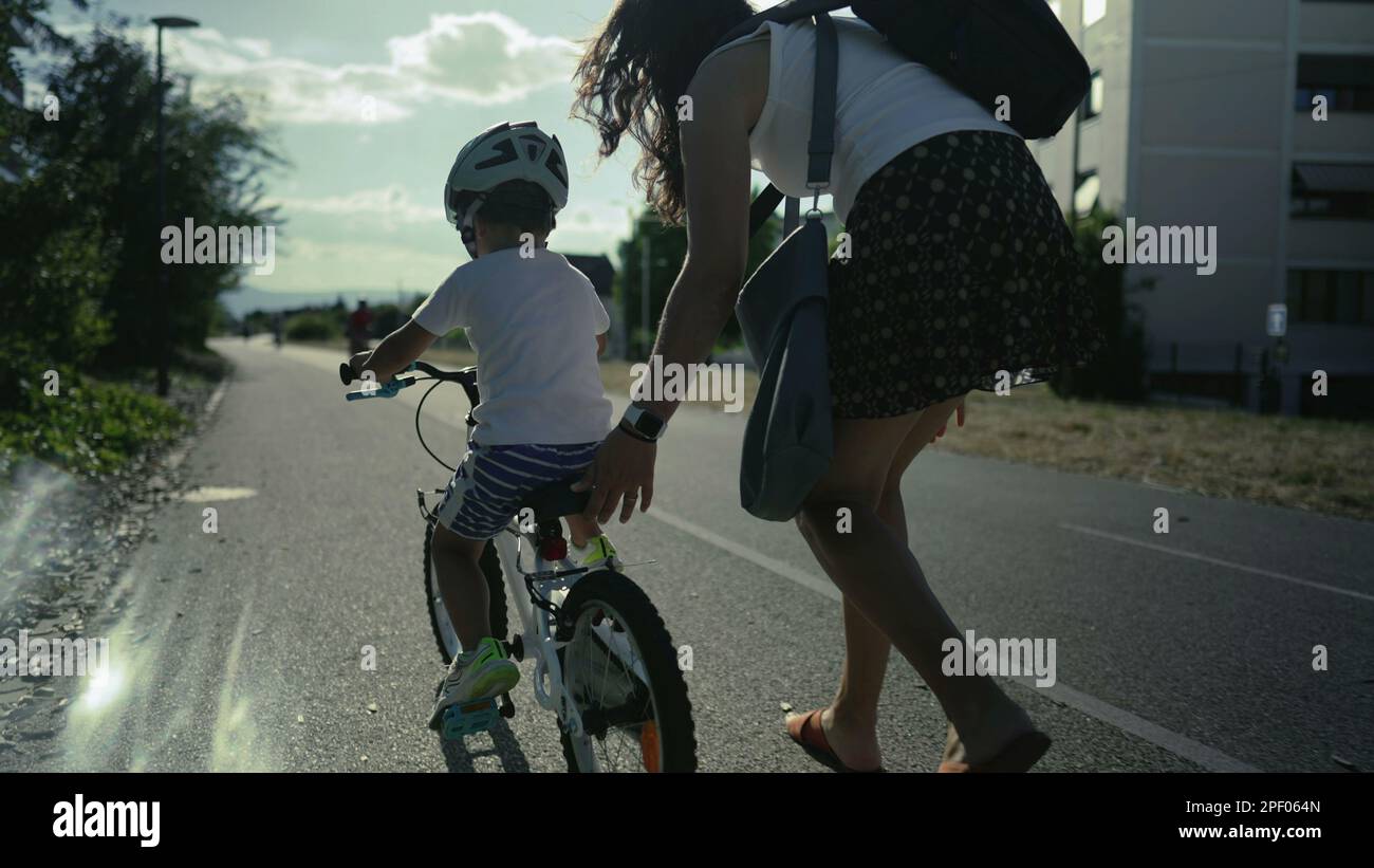 Back of child learning to ride bicycle outside with mother help and ...