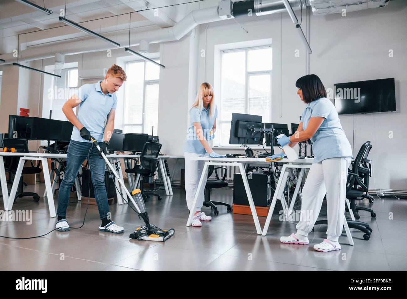 Cleans floor. Group of workers clean modern office together at daytime ...