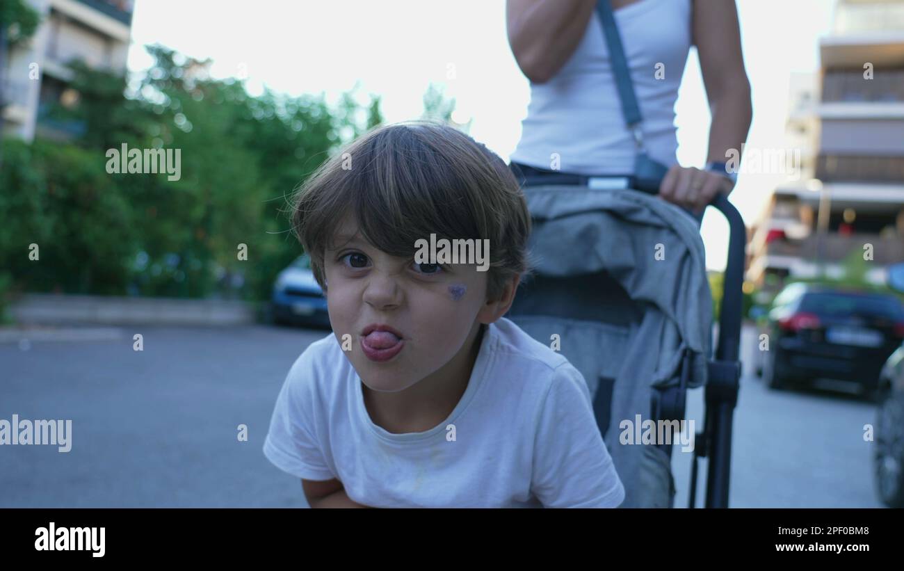 Goofy small boy sticking tongue out seated on stroller. Mischievous ...