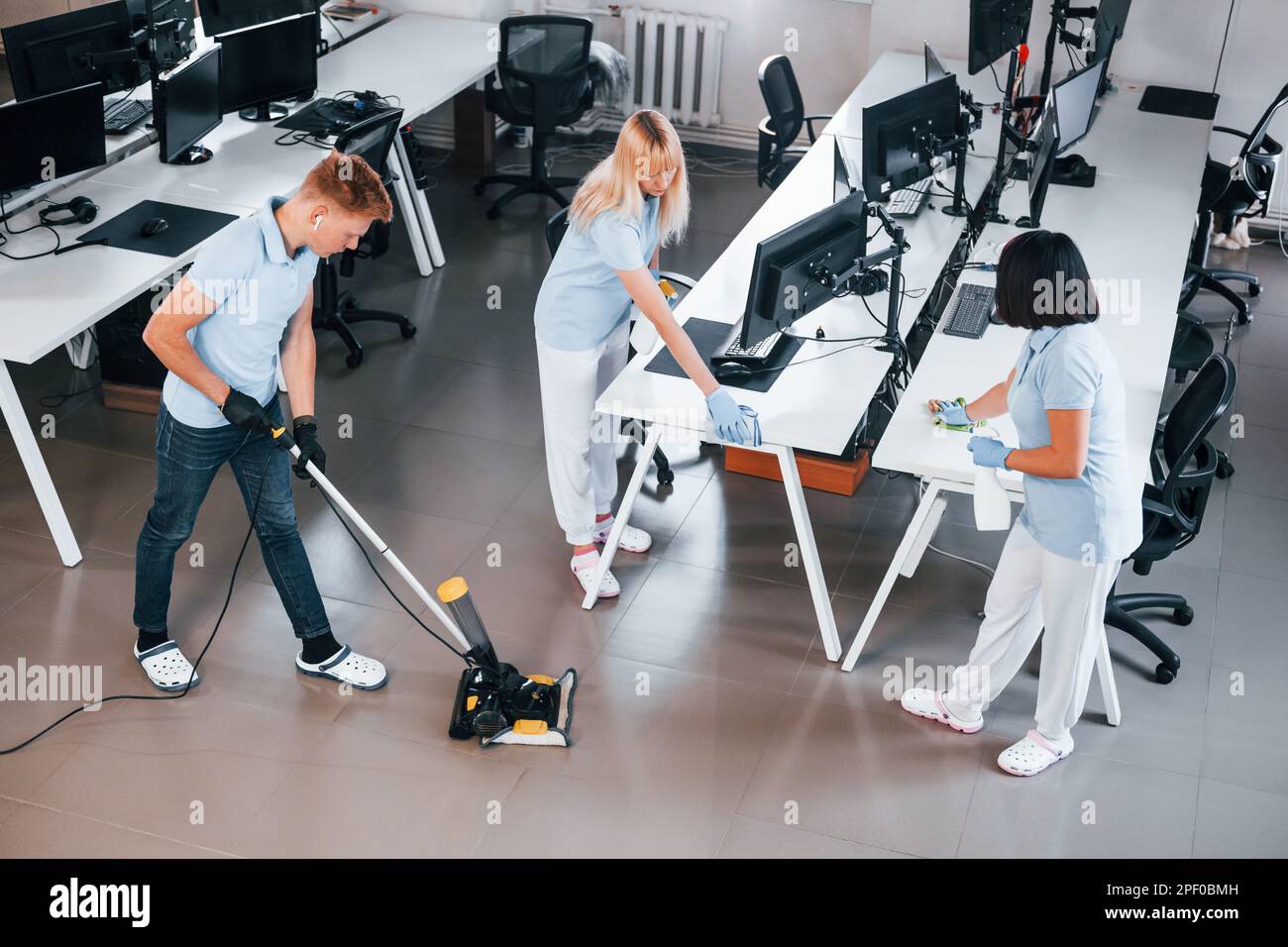 Cleans floor. Group of workers clean modern office together at daytime ...