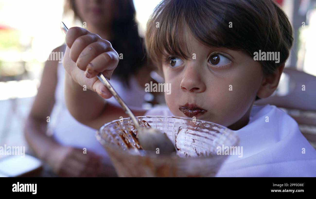 Cute little boy eating chocolate ice cream with spoon. Closeup face of ...