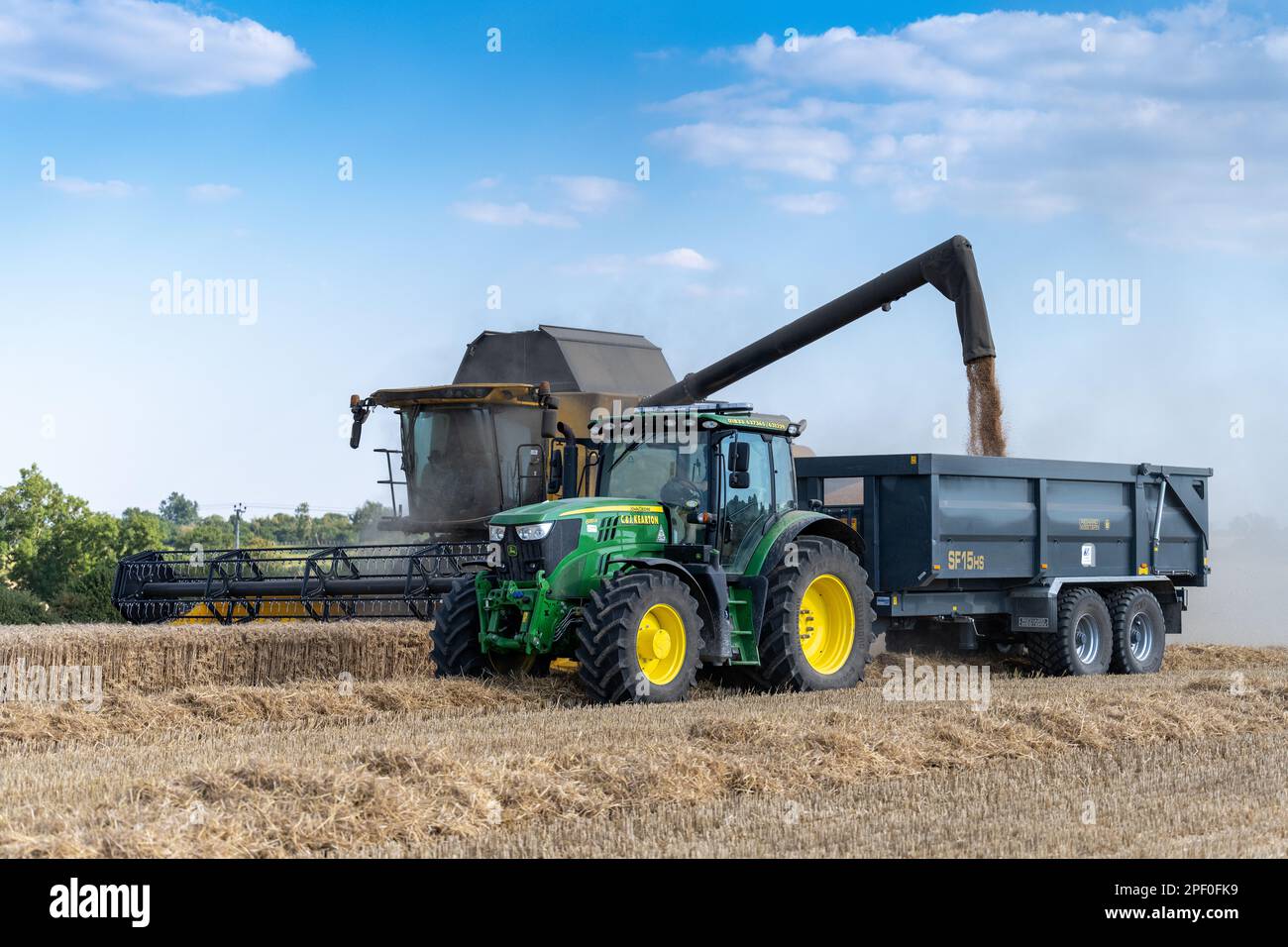 New Holland combine filling trailer with grain as it drives alongside ...