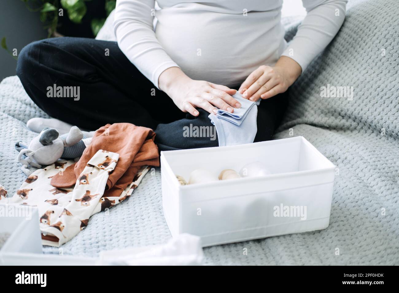 Pregnant Woman With Big Belly Holding Bodysuit And Sorting Clothes For