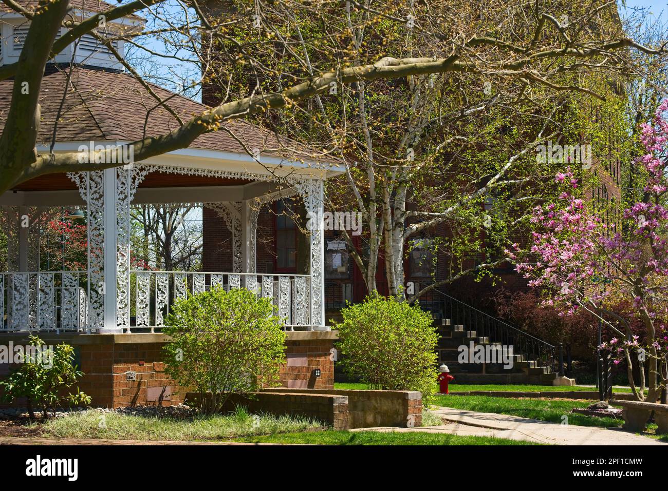 A gazebo with fancy decorative grillwork painted white stands on a ...