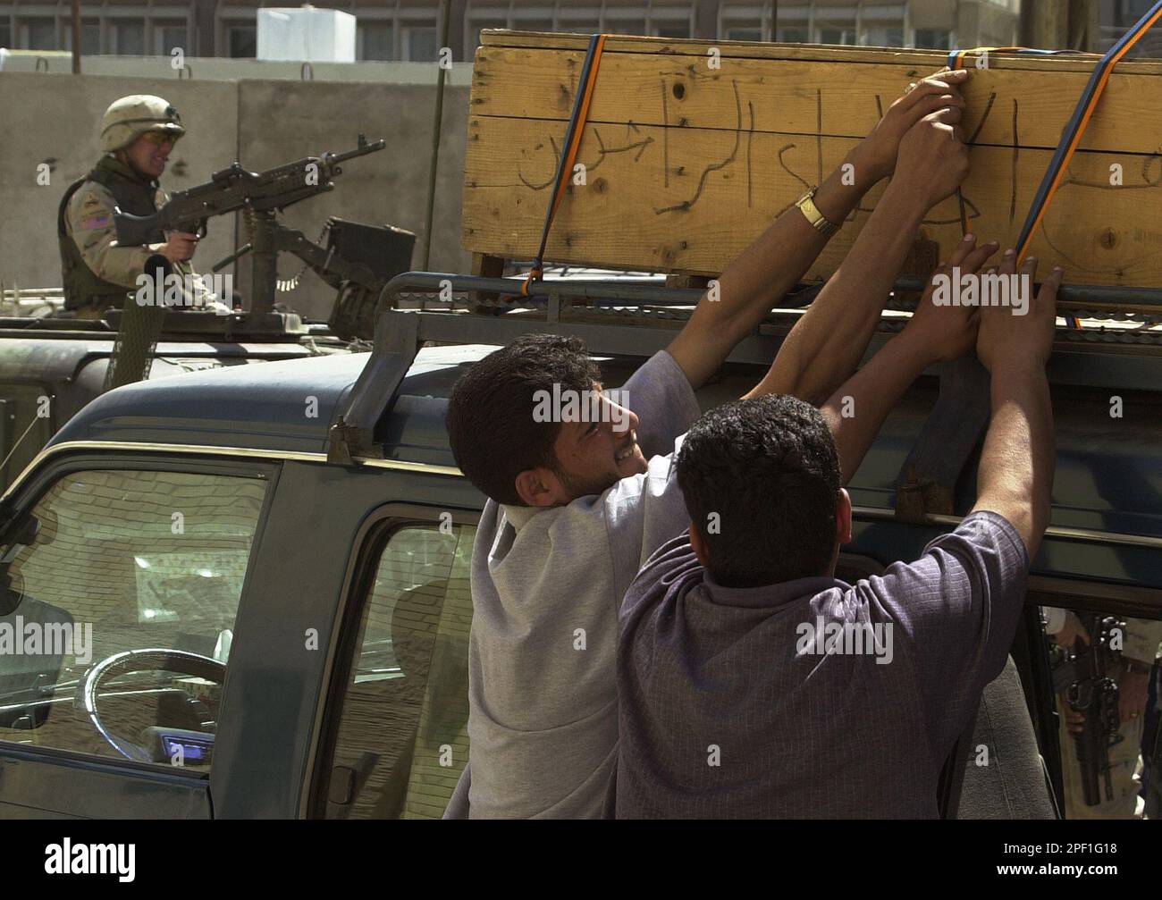 An American patrol rides by Iraqis securing the coffin containing the ...