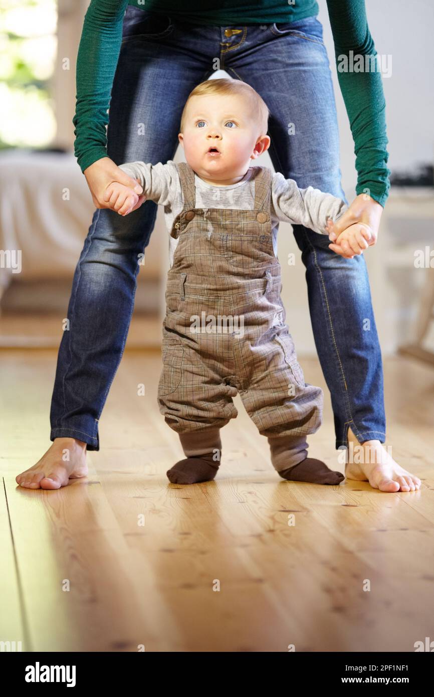 Taking those first steps. Young mom helping her baby boy learn to walk ...