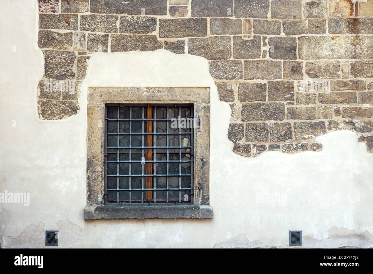 Square window with a metal grill against a partially plastered wall of ...