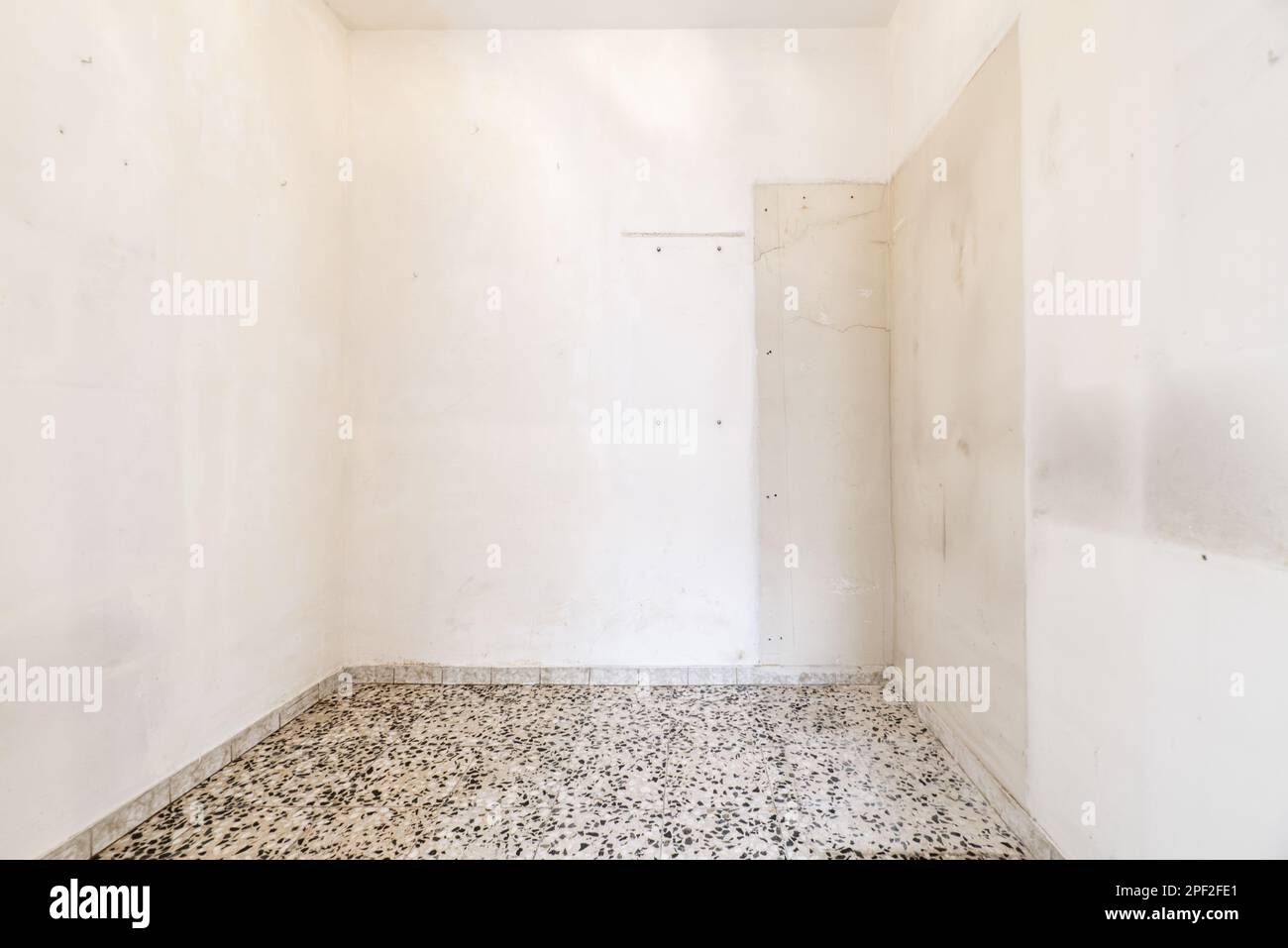 Empty living room with black dotted terrazzo floor and poorly painted ...