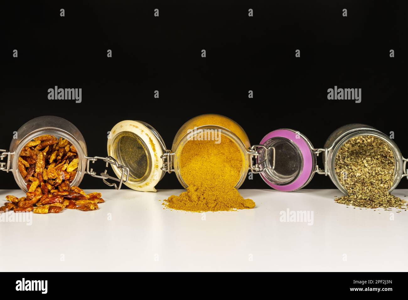 glass jars full of spices spilling their contents on a smooth white ...