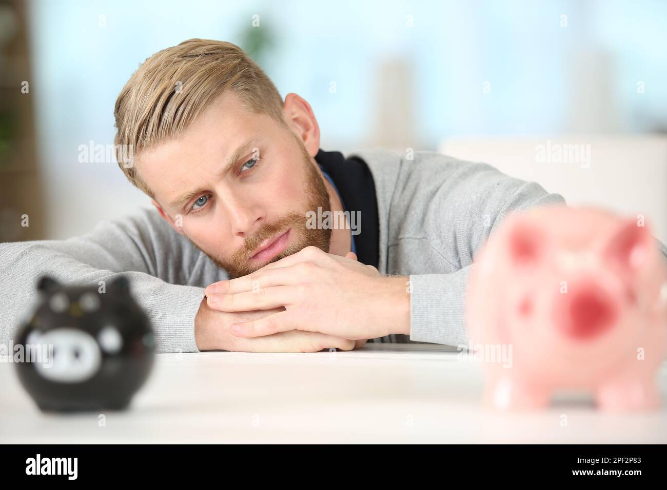 young man with piggy bank making serious face thinking Stock Photo - Alamy