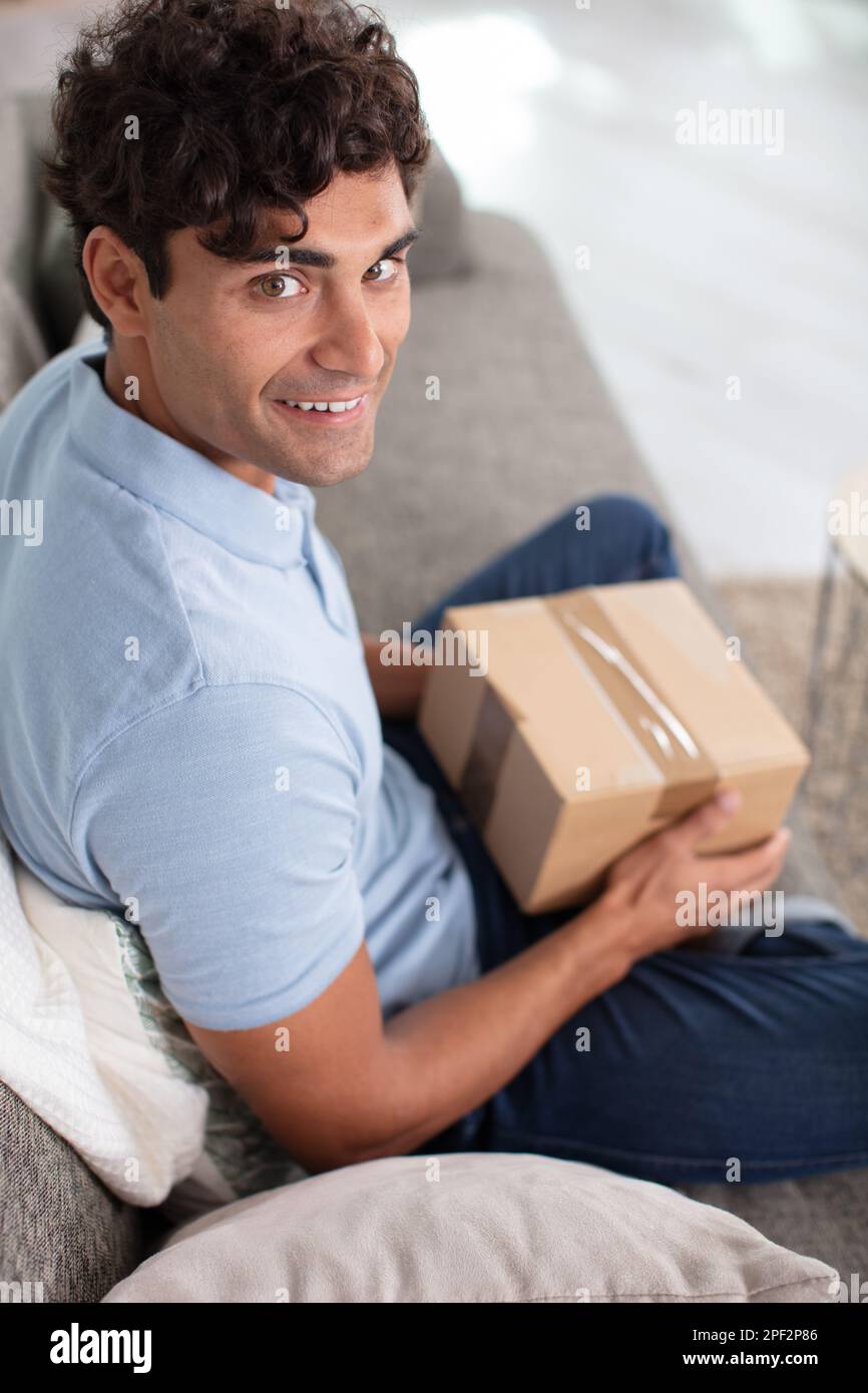 handsome young man opening parcel while sitting on sofa Stock Photo - Alamy