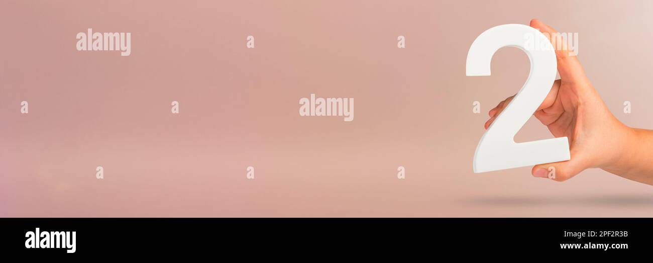 Number two in hand. Hand holding white number 2 on red background with ...