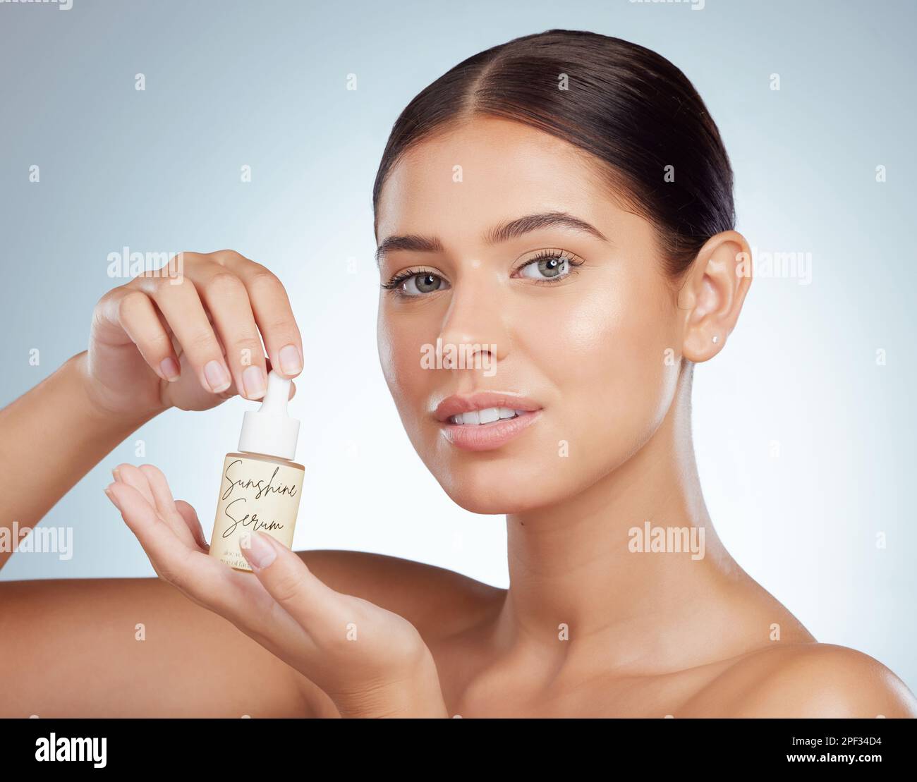 Portrait of beautiful woman holding face serum while posing with ...