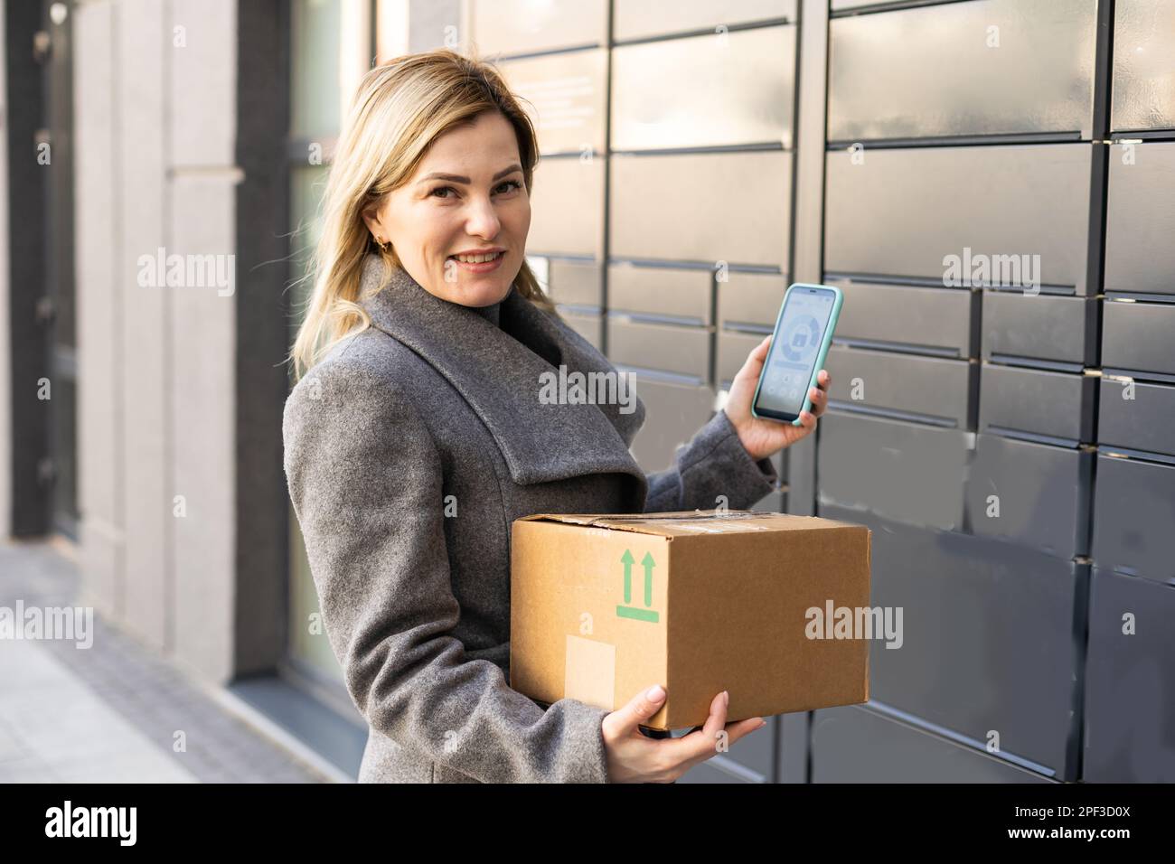Beautiful woman picking up a package from a smart electronic steel parcel locker box, automatic ...
