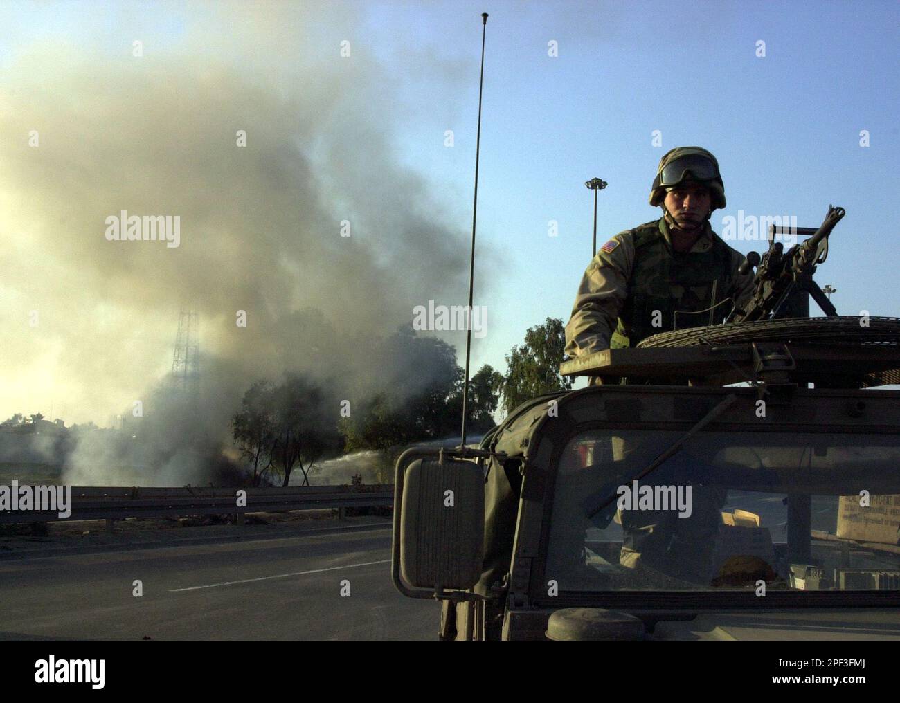 A U.S. soldier mans a machine gun on top of a humvee while smoke rises ...