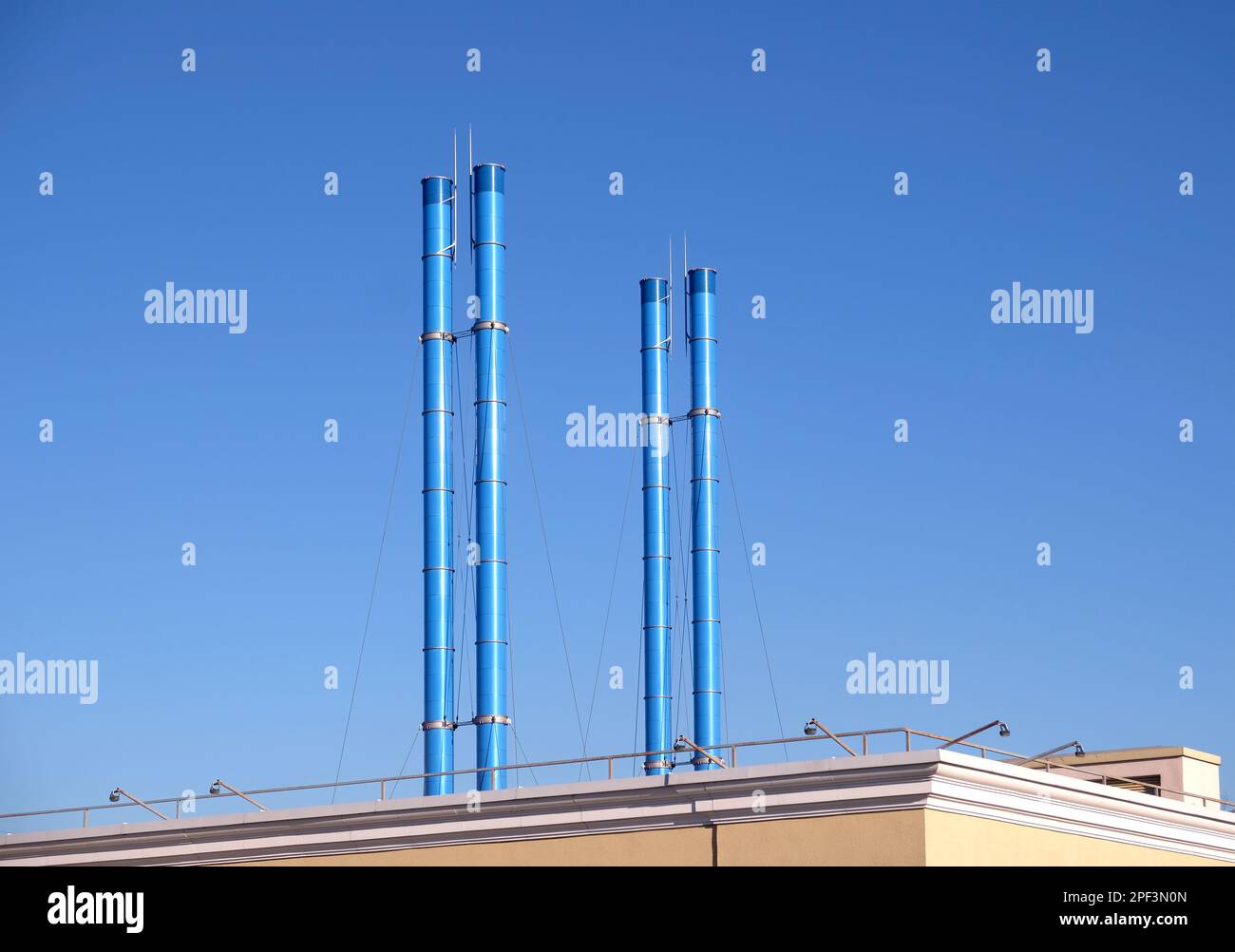 Four painted blue smoke stacks after roof of building on clear blue sky ...