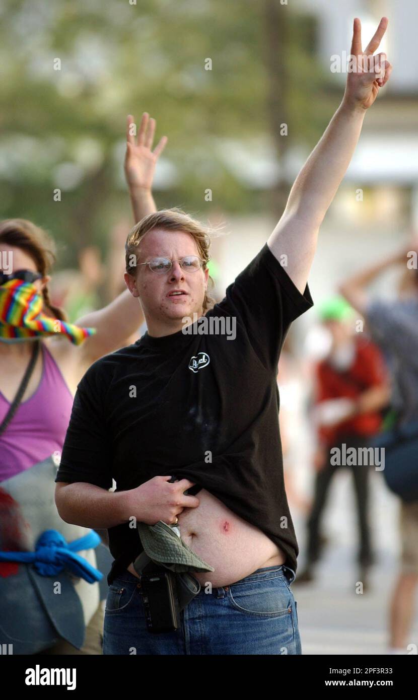A protester flashes the peace sign as he hold up his shirt showing a ...