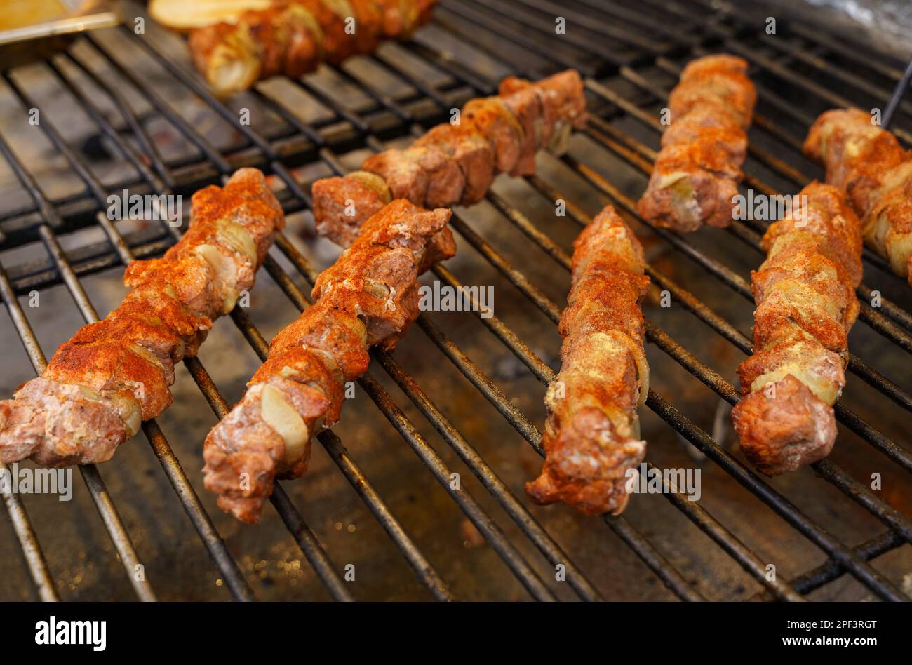 Fried meat with onions on a skewer lies on the grate. Polish street ...