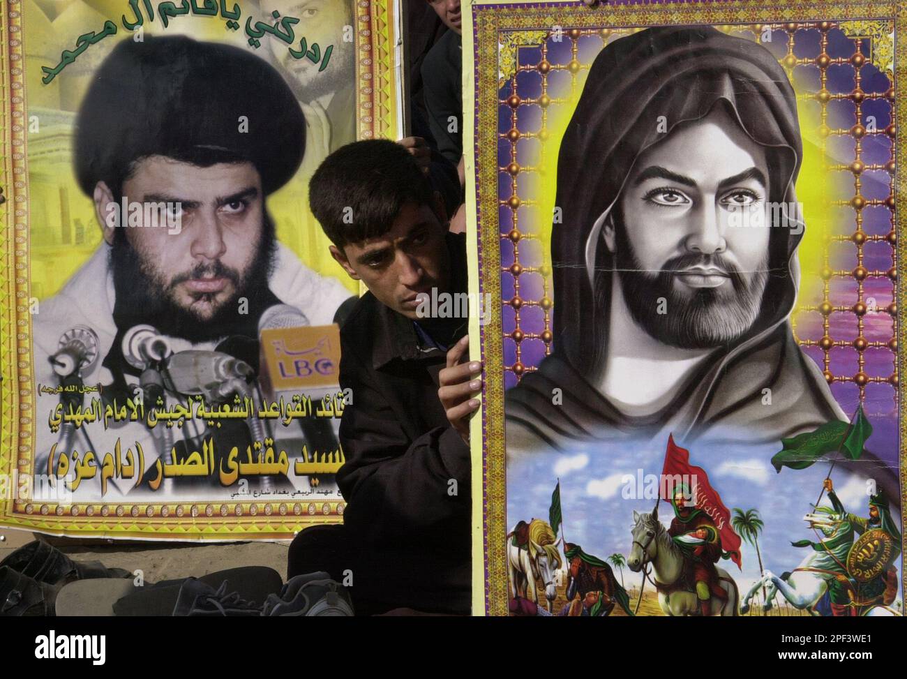 An Iraqi sits between posters of prominent Shiite cleric Sheik Muqtada ...