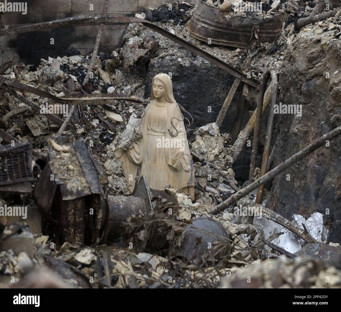 A statue of the Virgin Mary stands among the rubble of a burned-out ...