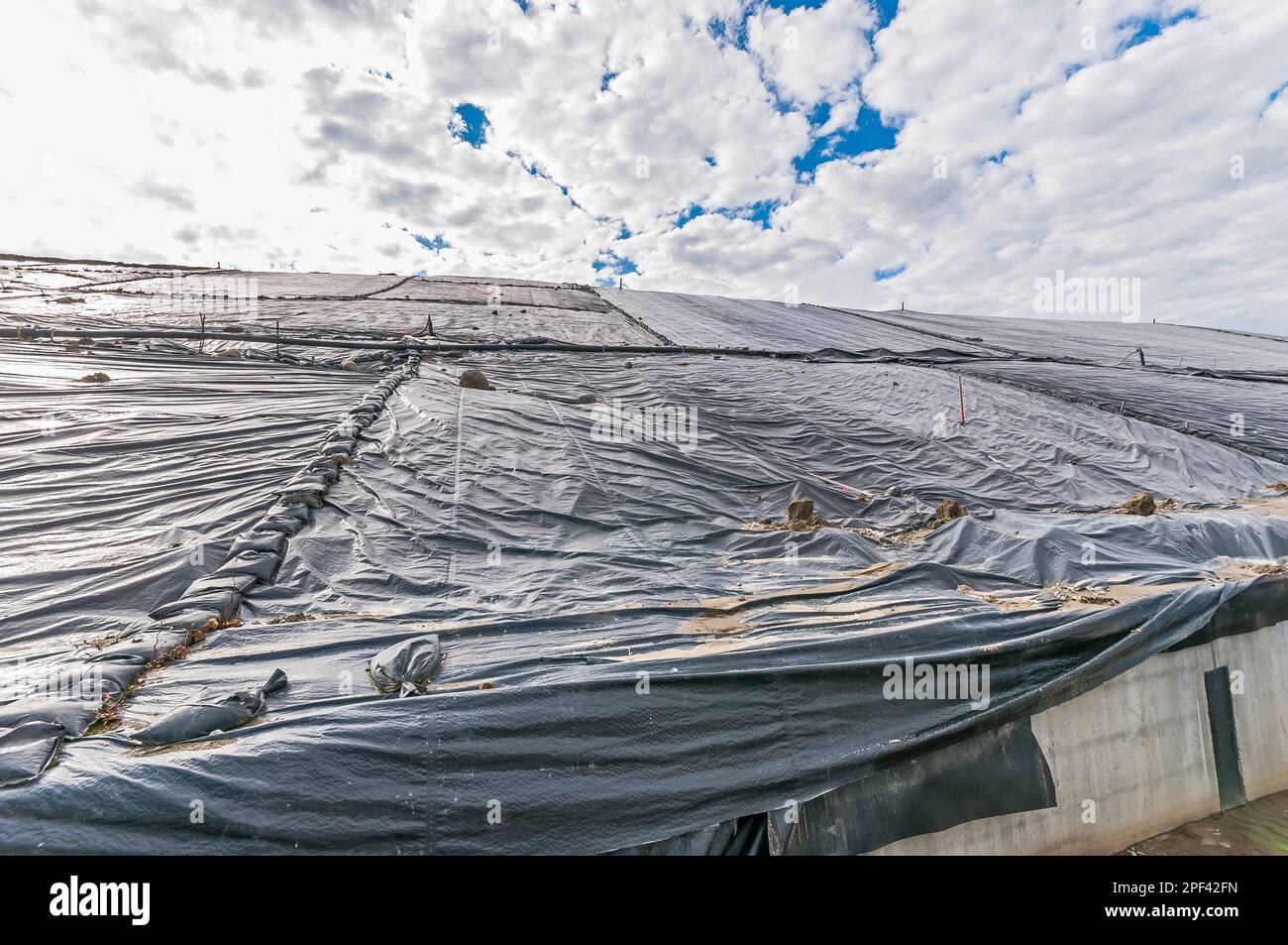 A concrete box culvert in the foreground with a geomembrane covering ...