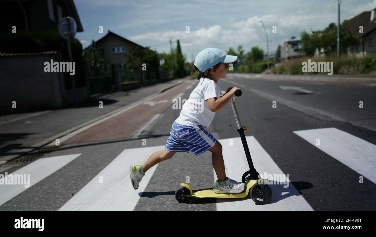 Little boy crosses street with toy 3 wheeled scooter. Pedestrian child ...