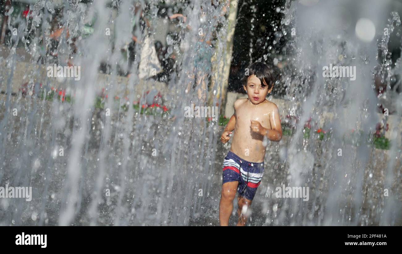 Little boy running at water jets in city park during summer day. Small ...