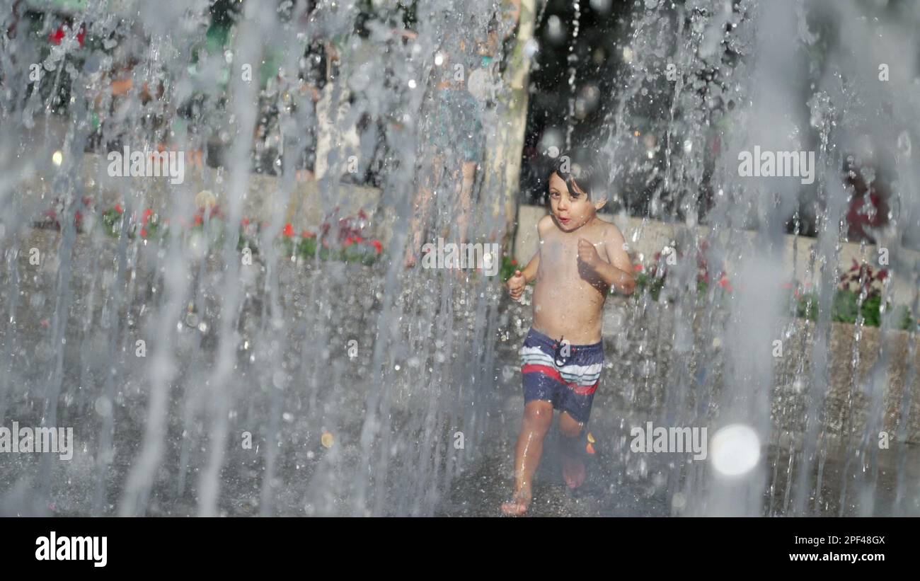 Little boy running at water jets in city park during summer day. Small ...