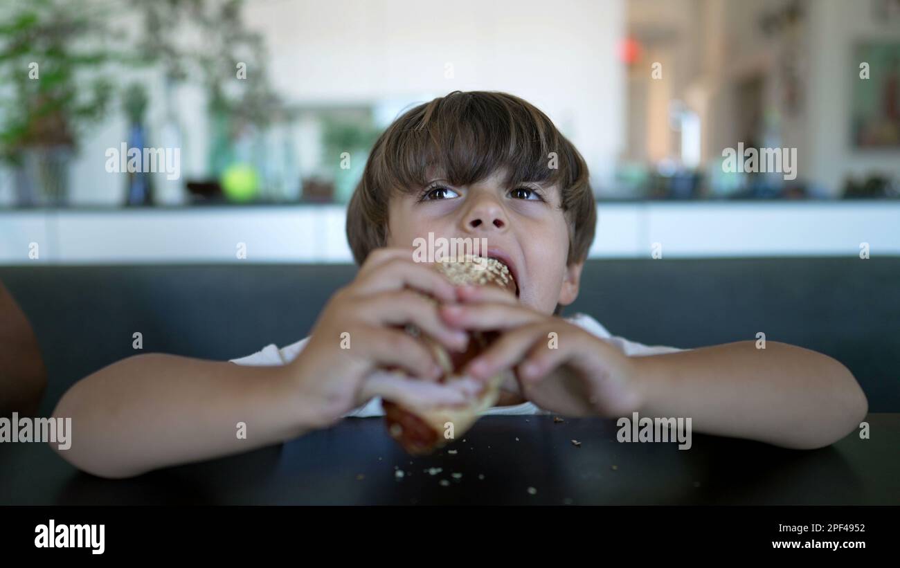 One little boy grabbing bread taking a bite of carb food seated at ...