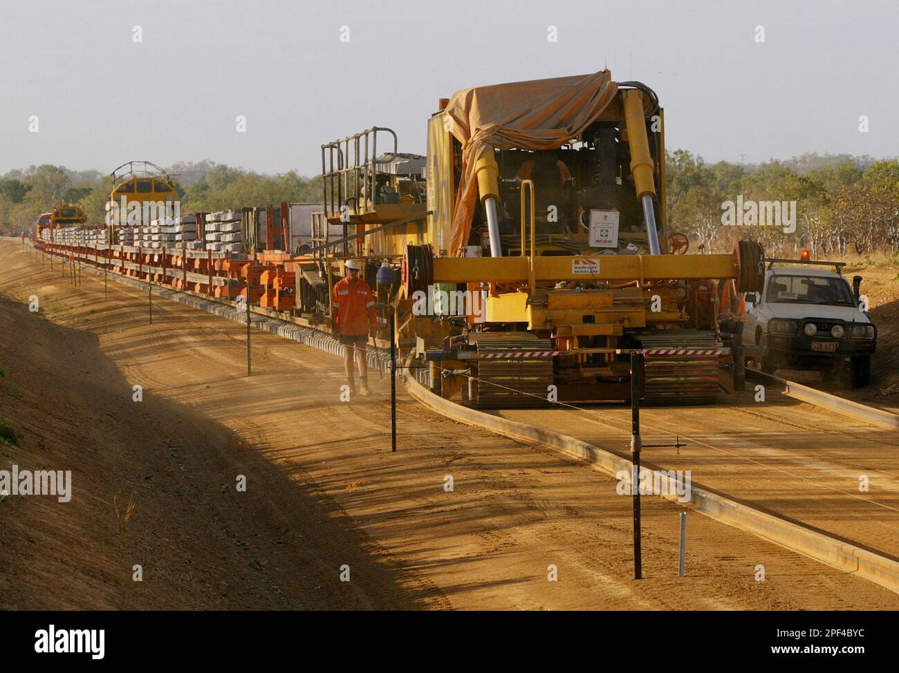 Workers walk beside a track laying locomotive as it lays rail track on ...